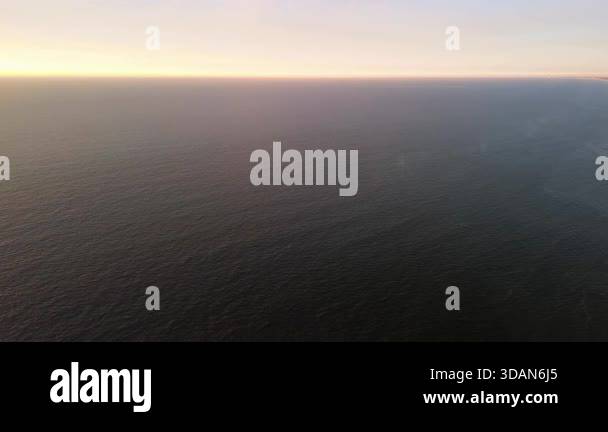 Vast ocean under softly lit sky at sunset, horizon divides rippled ...