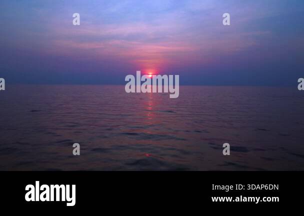 Sun dipping below the horizon reflecting on the calm water at dusk ...