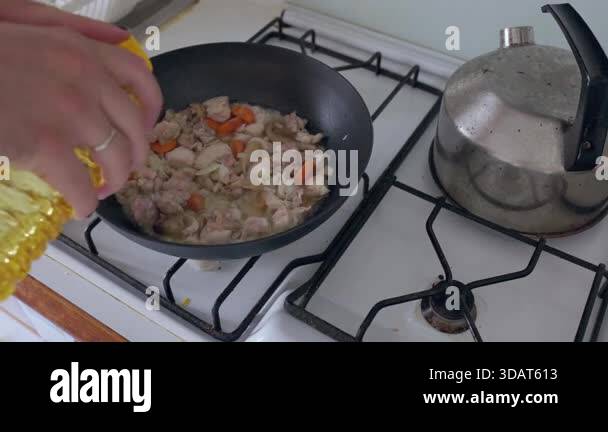 Chef pouring sunflower oil into a wok while cooking a chicken and ...