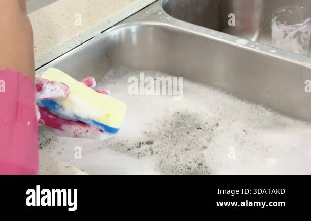 Person wearing pink gloves scrubs and rinses dirty plates with a sponge ...