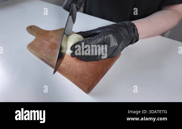 Close-up of a person's gloved hands meticulously cutting a raw onion ...