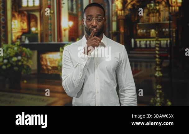 Man wearing white shirt and glasses with finger to lips for silence in ...