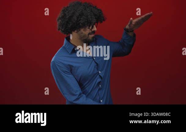 Man with curly hair and glasses raising right hand palm down while ...