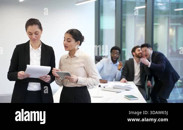 Group of male employees whispering behind two female coworkers in ...