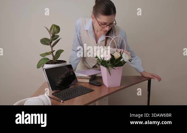 Office worker standing by her desk, leaning in to gently smell a ...