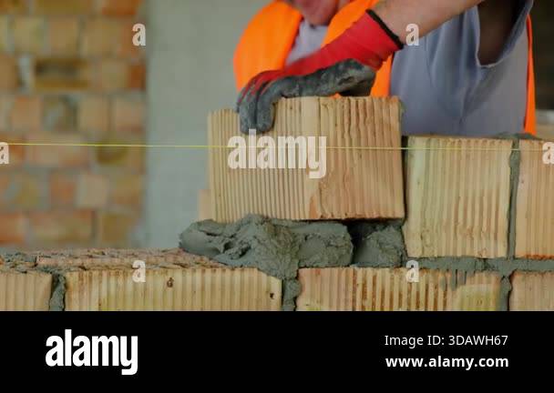 Builder lays bricks creating wall at construction site. Contractor ...