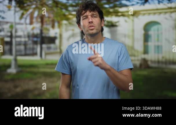 Man with finger on lips gesturing silence in a sunny green park setting ...