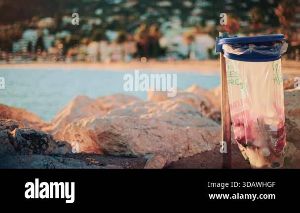 Transparent trash bag filled with waste hanging on a bin by rocky sea ...