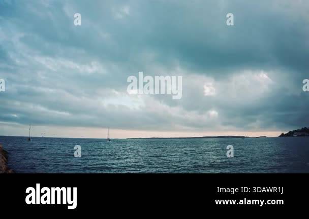 Wide shot of the sea under large clouds, with small sailboats in the ...