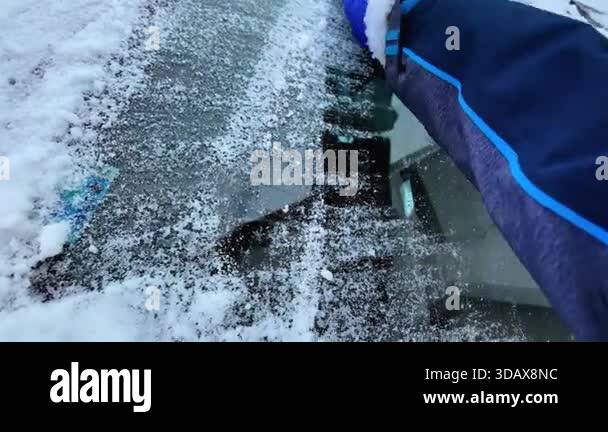 Scraping snow and ice from a car windshield with a plastic tool ...