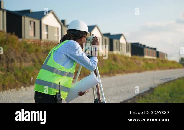 African american surveyor in a safety vest and hard hat using a ...