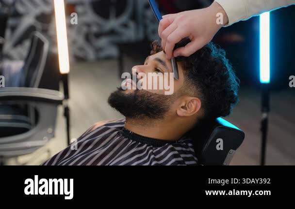 Relaxed man with a curly hairstyle getting his beard shaped by a ...