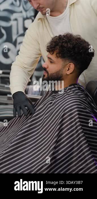 Professional hairstylist finishing work on a male client, removing the ...