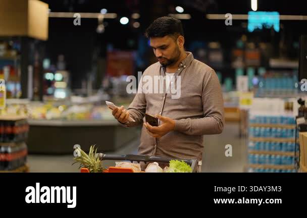 Young indian man standing in a grocery store aisle with a shopping cart ...