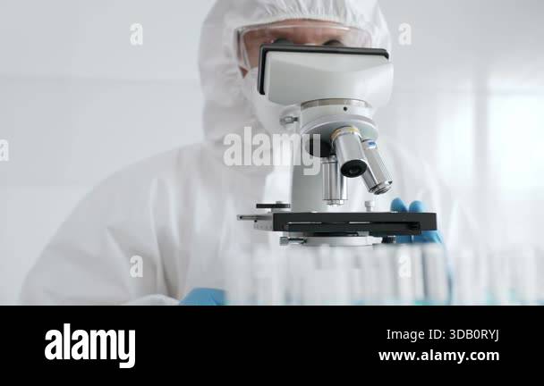 Scientific researcher wearing protective gear adjusting microscope ...