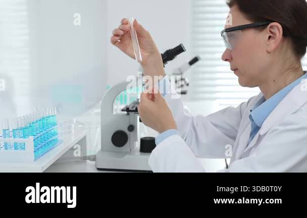 Female scientist wearing lab coat and protective glasses analyzing test ...