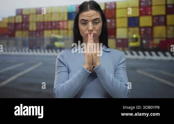 Woman praying outdoors at a port with colorful shipping containers ...