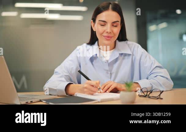 Positive woman diligently works, writing notes with pen in bright ...