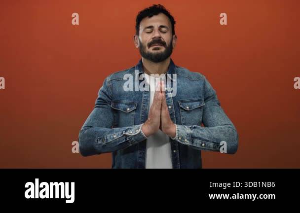 Hispanic man meditating with a beard and denim jacket against an orange ...