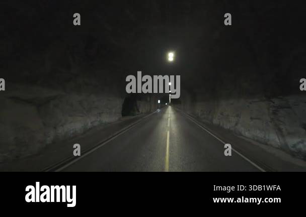 Slow-motion vehicle view inside a long tunnel with wet pavement and dim ...