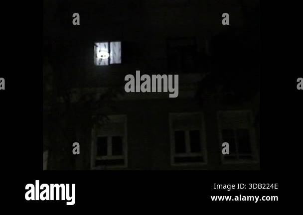 Nighttime view of dark building facade with one illuminated window ...