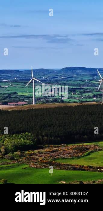 The wind turbines are situated on a hilltop overlooking a lush green ...