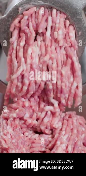 Vertical video. Minced pieces of meat slowly comes out of grinder and ...
