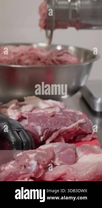 Cook uses knife to cut meat on table in kitchen of production facility ...
