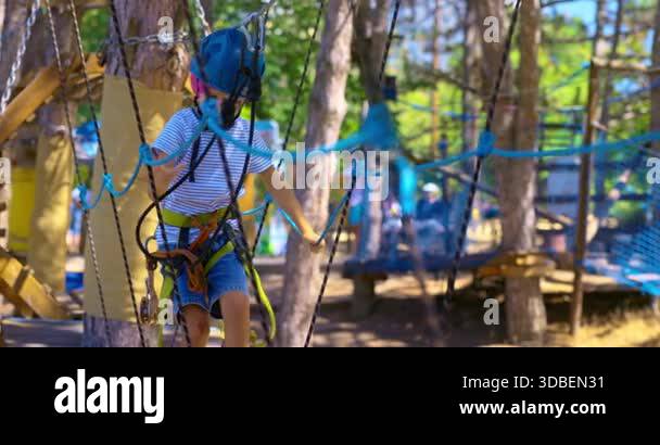 A child wearing a helmet and harness navigates a challenging rope ...