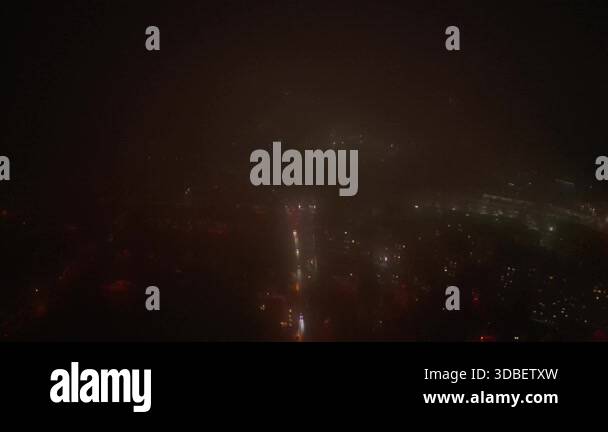 Steady 4K drone shot at night above a city wrapped in heavy fog ...