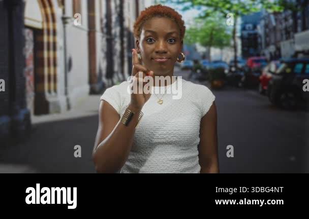 Young african american woman places finger to lips for silence on busy ...