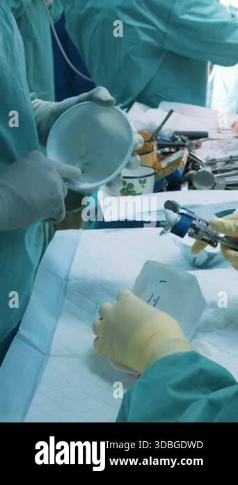 Surgeon's gloved hands preparing bone cement in a small bowl with a ...