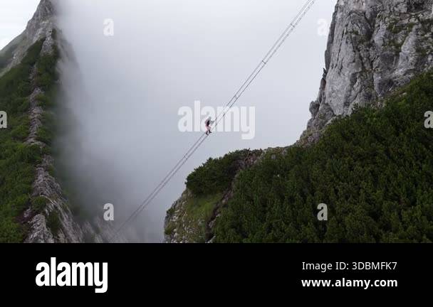 Aerial view of a brave mountaineer carefully crossing a suspended ...