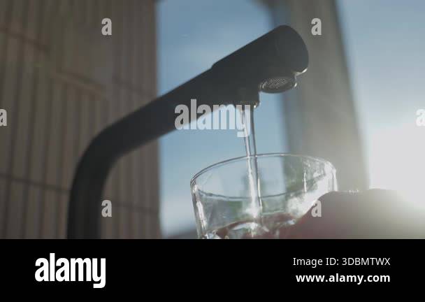 Hand holding glass under black kitchen faucet with sunlight from window ...