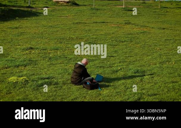 Man working on laptop on green grass in open field. Freelancer typing ...