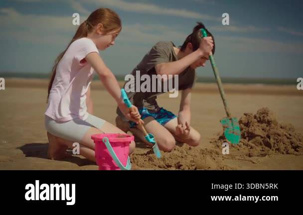 Girl digging sand with small spade while boy working with big shovel ...