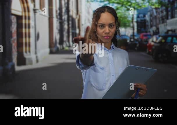 Woman shows middle finger while holding a clipboard and pen on a city ...