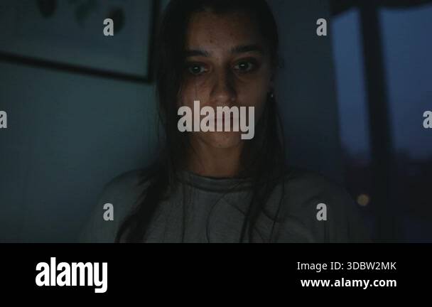 solemn woman lit by laptop glow, direct stare and steady breathing ...