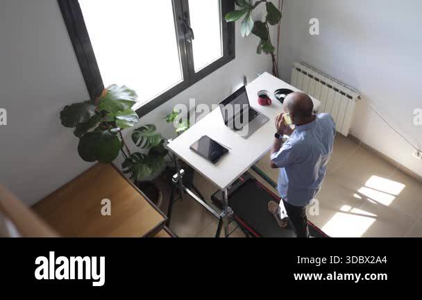 bold man walking on a treadmill at the desk with gadgets. pots with ...
