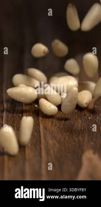Pine nuts drop onto a wooden surface, showing their natural shape and ...