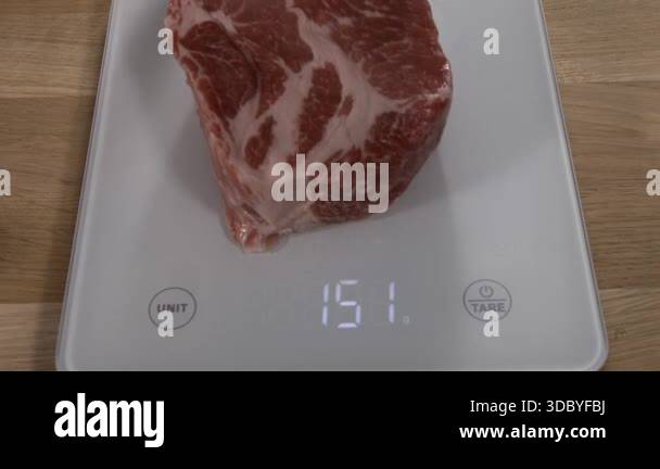 A person places a piece of meat on a kitchen scale to measure its ...