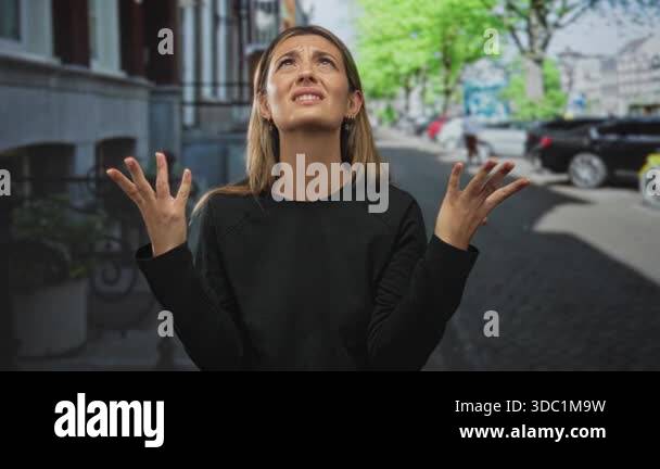 Young woman raising both hands with palms visible and furrowed brow on ...