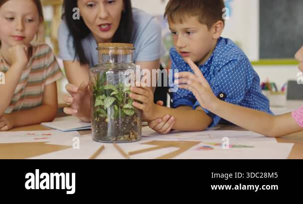 Female teacher showing a terrarium plant in a glass jar to a group of ...