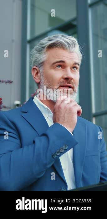 Mature businessman working thoughtfully on a laptop outdoors with a ...