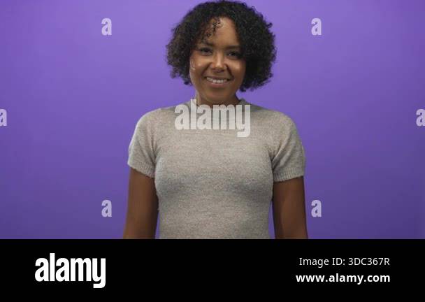 Woman smiling with visible teeth and curly hair in purple studio ...