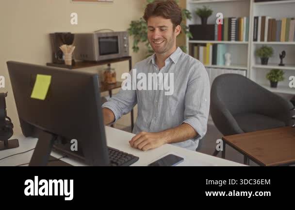 Man takes selfie with smartphone while seated at desk, using desktop ...