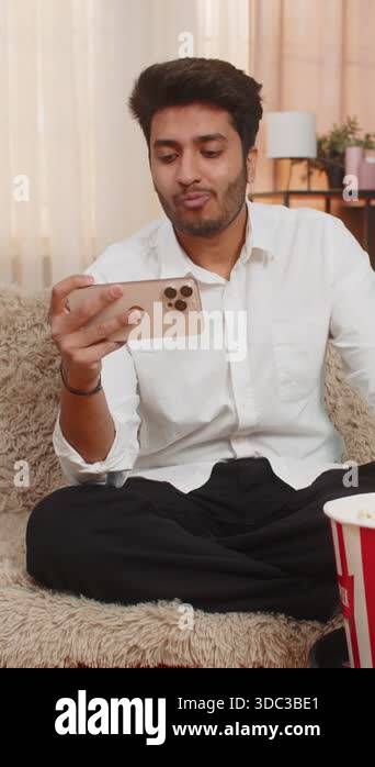 Indian man at home eating popcorn, deeply engaged in watching a movie ...