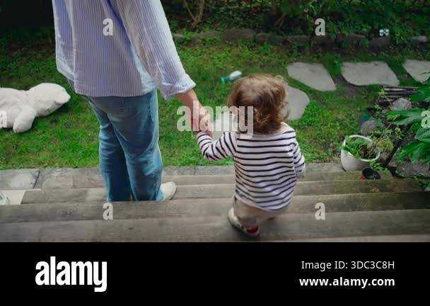 Toddler holding mother hand while stepping down wooden stairs into ...