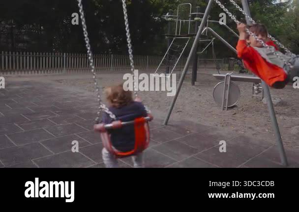 A toddler swings next to an older sibling, both moving at different speeds while sharing the ...