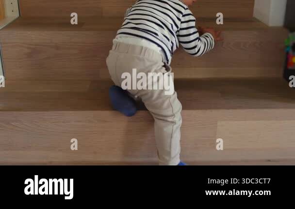 A toddler descends the stairs by sliding down feet first, lowering ...